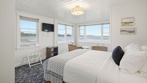 Quarto com cama, televisão, escrivaninha e vista para a praia.
