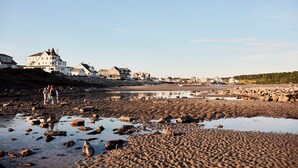 Uma área costeira com casas à beira-mar, uma praia de pedras e um corpo d'água calmo.