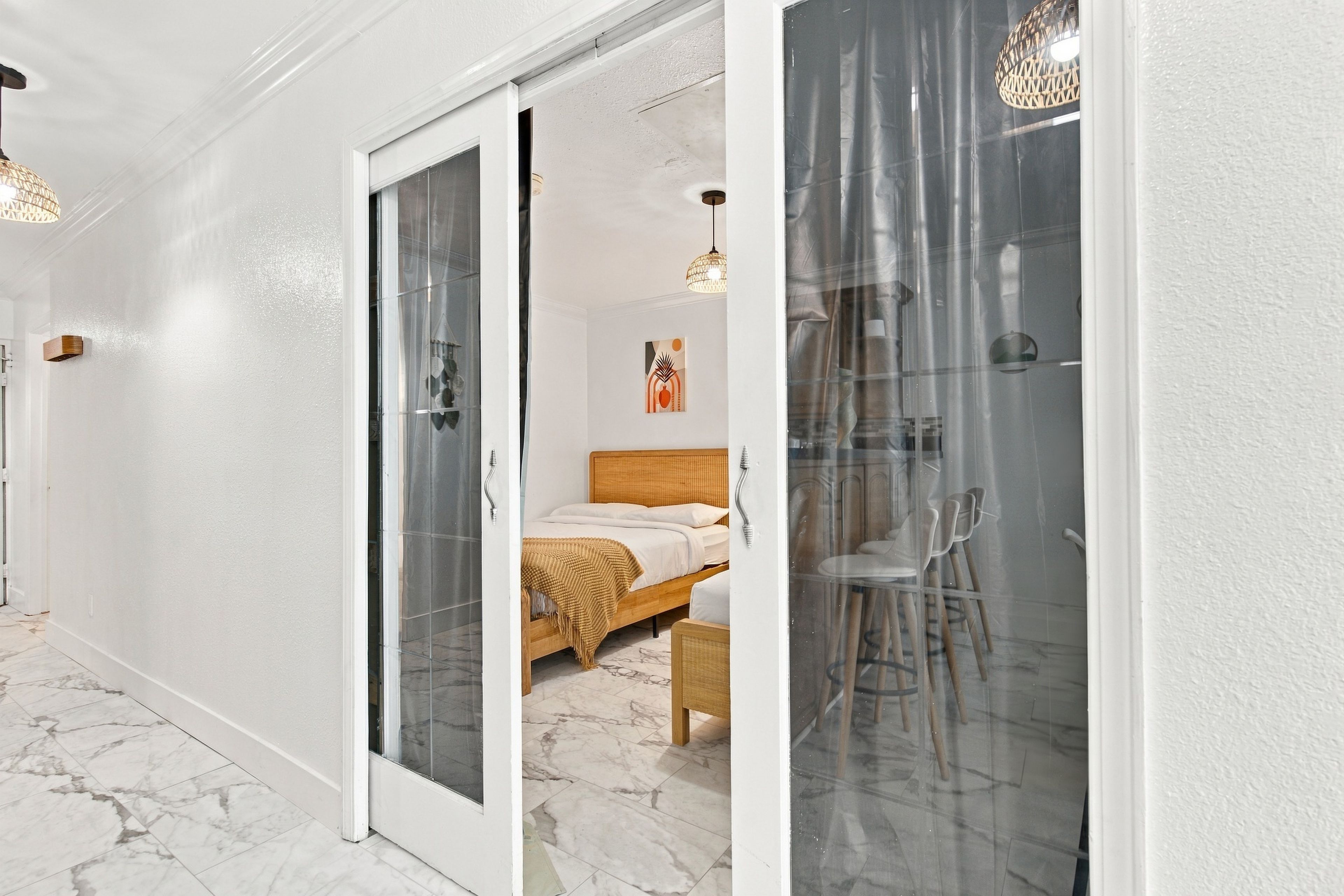 Quarto moderno com porta de vidro para um banheiro, cama de madeira e área de refeições com cadeiras.