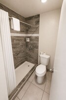 Casa de banho com chuveiro, sanita e um porta-toalhas.