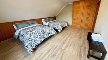 Quarto com duas camas, piso de madeira, guarda-roupa e um banquinho.