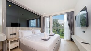 Quarto de hotel moderno com uma cama grande, uma televisão fixada na parede e uma janela com cortinas.