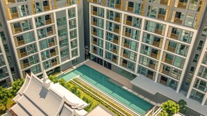 Um edifício moderno alto com várias varandas, uma piscina central e áreas verdes ao redor.
