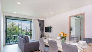 Uma sala de jantar moderna com uma mesa grande posta para quatro pessoas, cadeiras estofadas cinzentas e vista para o verde através das portas de vidro.