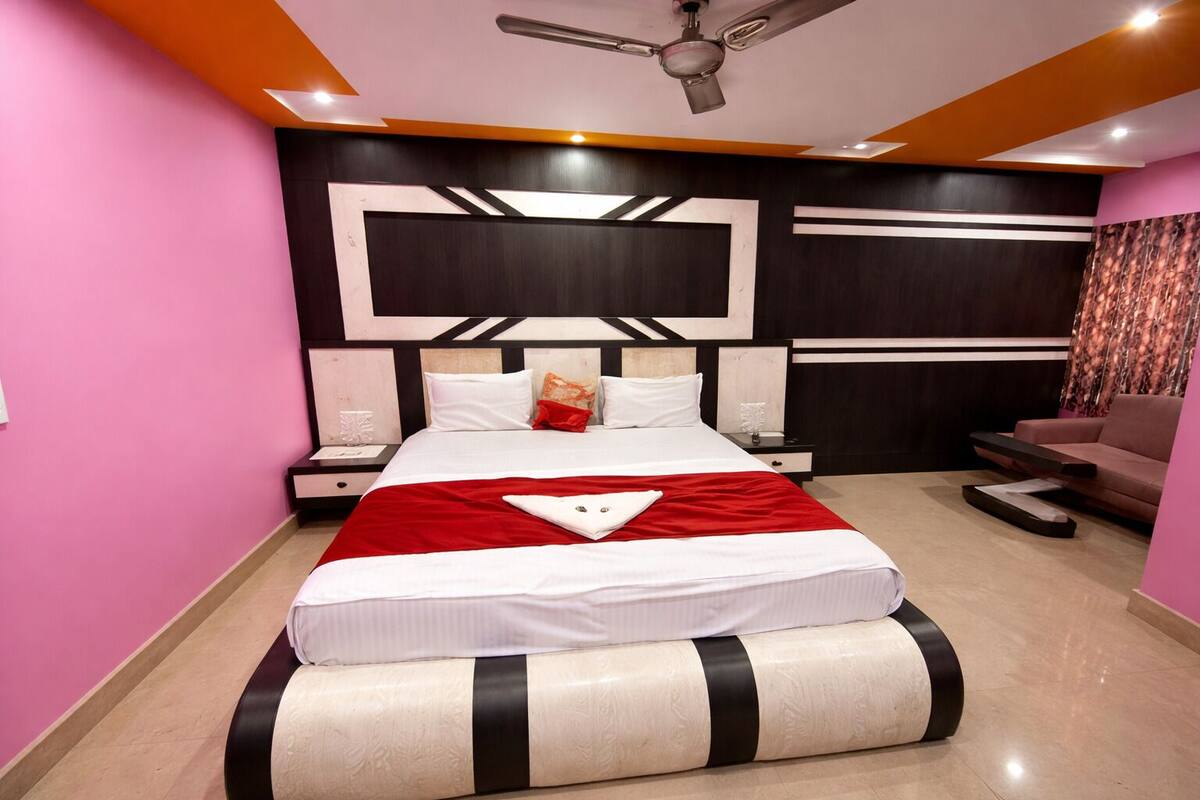 Quarto moderno com cama, mesas de cabeceira, sofá e ventilador de teto.