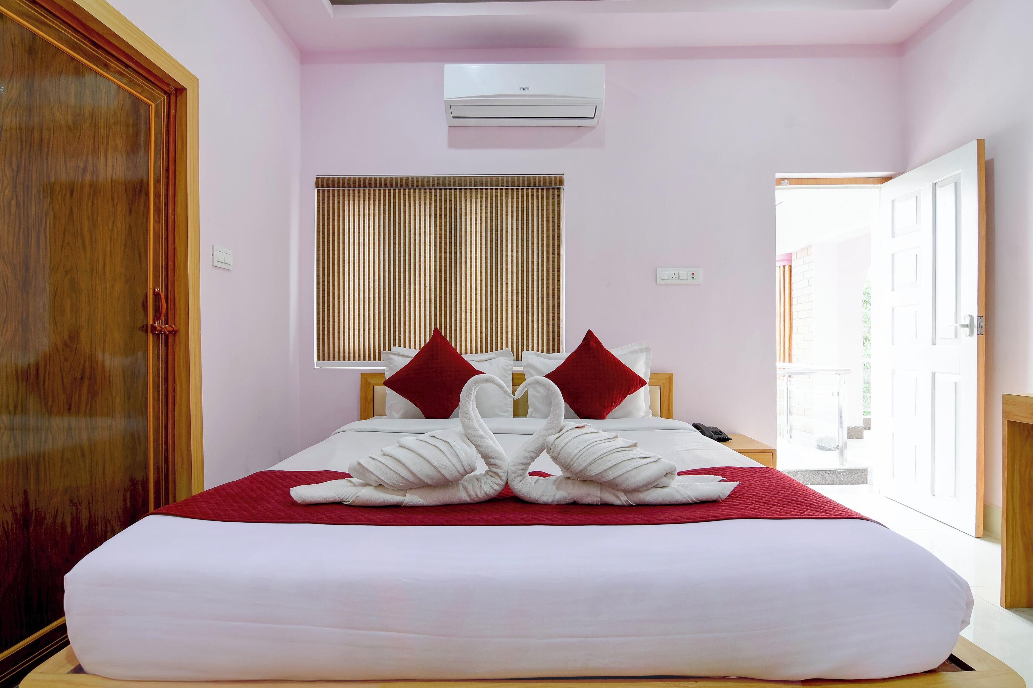 Quarto de hotel com cama, guarda-roupa de madeira, janela com persianas, unidade de ar condicionado e porta para o exterior.