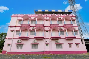 Um edifício rosa com várias varandas, aparelhos de ar condicionado e uma torre de eletricidade visível.