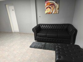 Quarto com sofá de couro preto, tapete cinza e uma pintura abstrata colorida na parede.