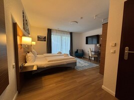 Quarto de hotel com cama, escrivaninha, cadeira, televisão e janela com cortinas.