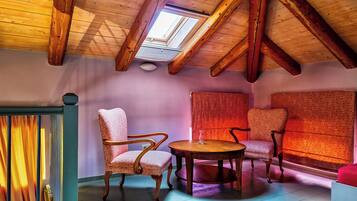 Um quarto de sótão acolhedor, com vigas de madeira, um claraboia e duas poltronas estofadas ao redor de uma mesa pequena.