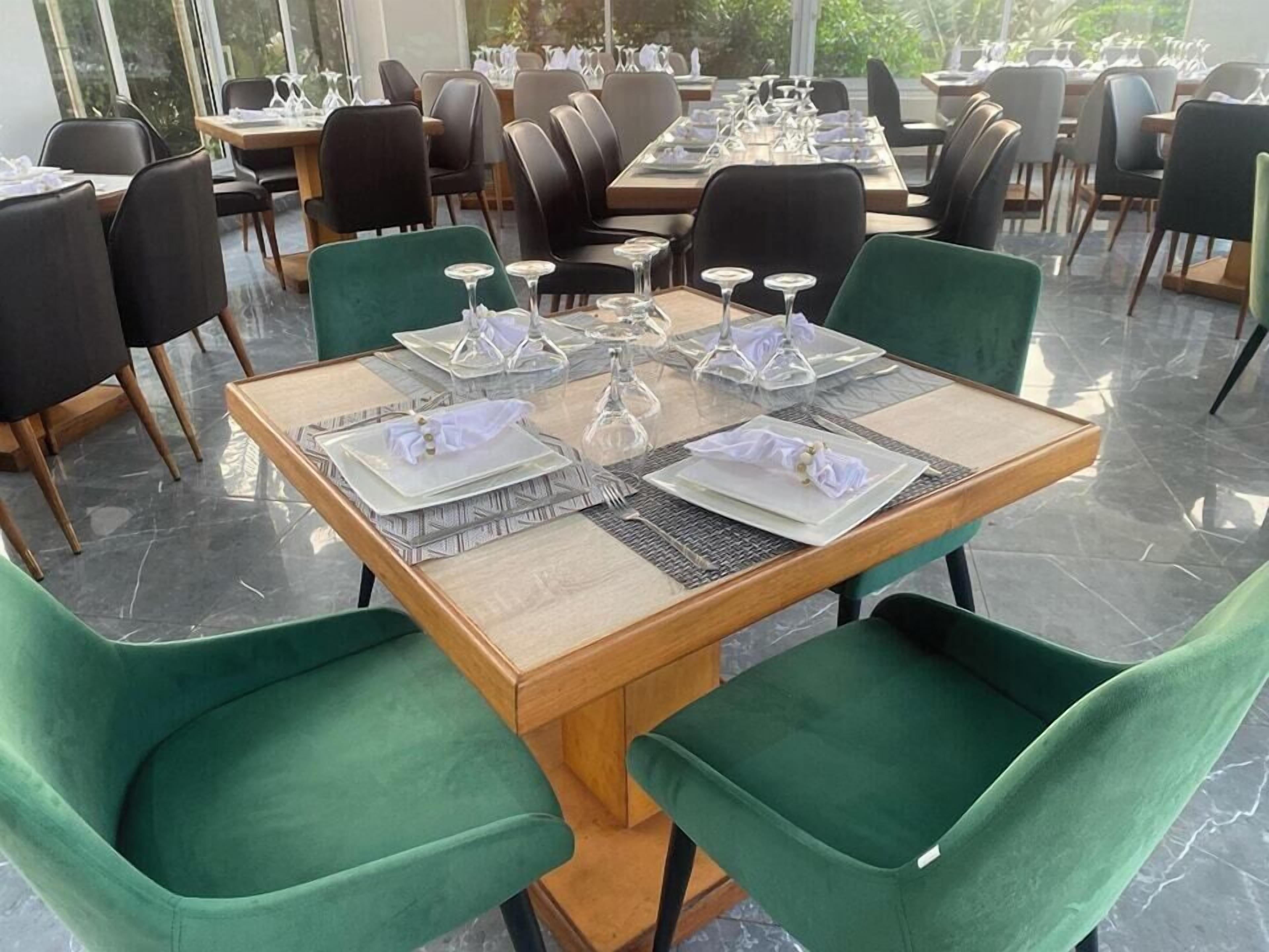 Restaurante com cadeiras e mesas estofadas em verde, preparadas para refeições.