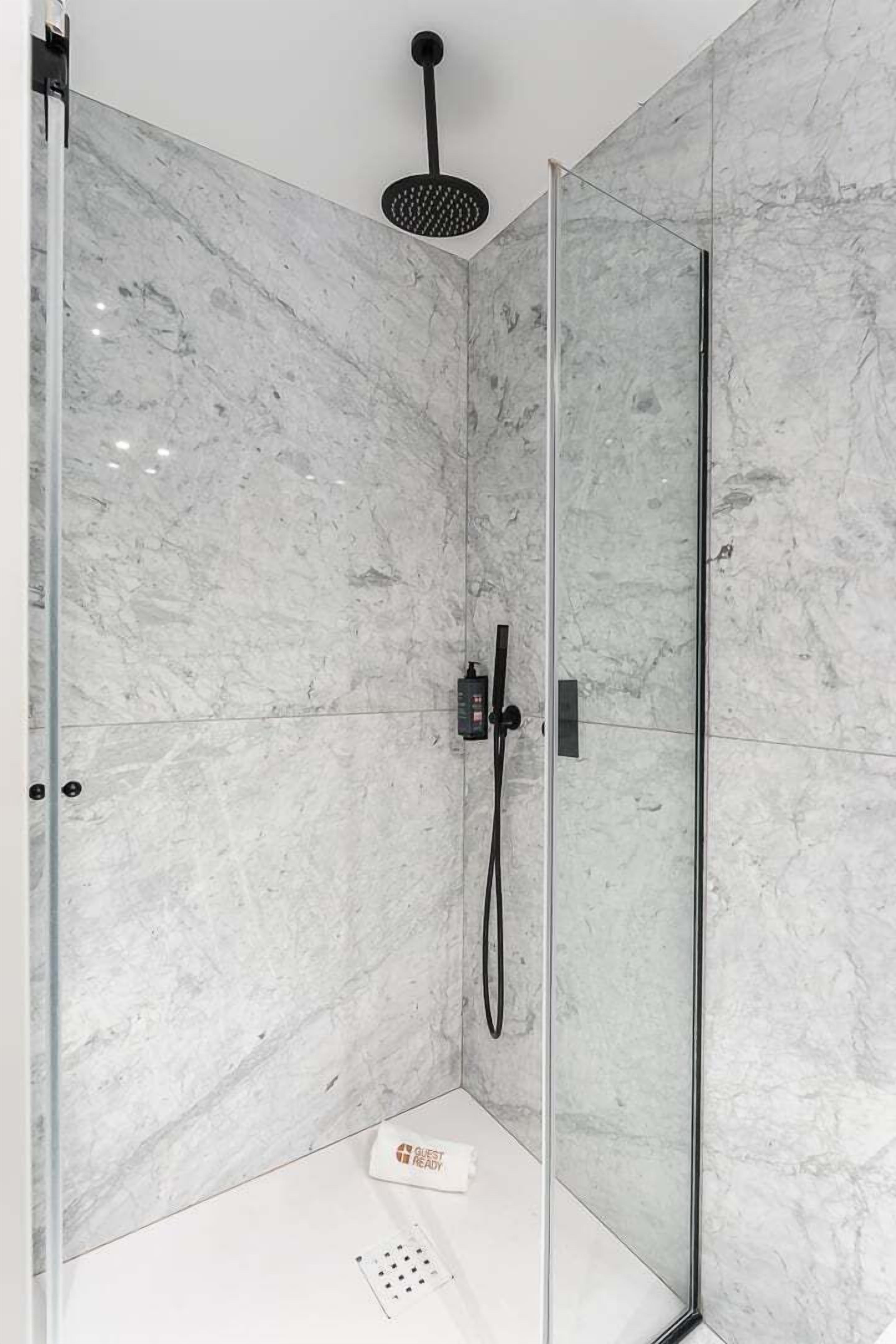 Um chuveiro moderno com um chuveiro de mão, portas de vidro e um painel de controle.
