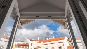 Janela aberta com vista para edifícios e um céu parcialmente nublado.
