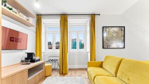 Uma sala de estar moderna com um sofá amarelo, uma máquina de café, uma televisão e uma janela com cortinas amarelas.