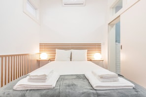 Quarto de hotel com uma cama grande, duas luminárias de cabeceira, um painel de madeira na cabeceira e um tapete cinza.