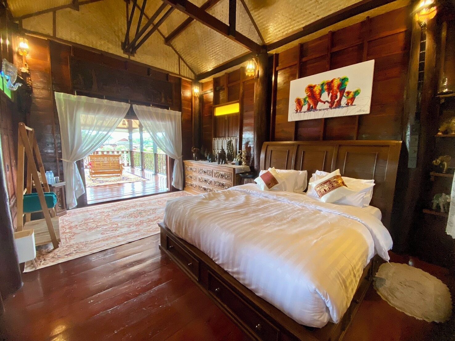 Quarto espaçoso com cama grande, piso de madeira, varanda com vista e uma pintura na parede.