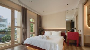 Quarto de hotel com uma cama grande, uma cadeira vermelha, banheiro com espelho e vista para o exterior.