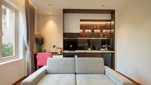 Uma sala de estar moderna com sofá, cozinha equipada com armários e eletrodomésticos, e uma janela com cortinas.