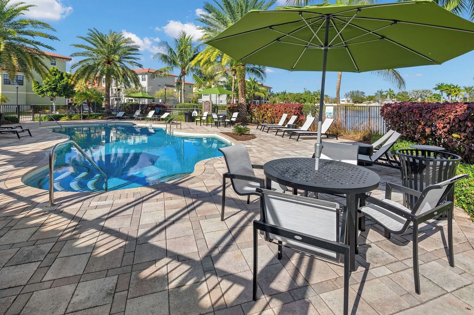 Uma área de piscina com uma piscina azul cristalina, espreguiçadeiras e uma mesa com cadeiras.
