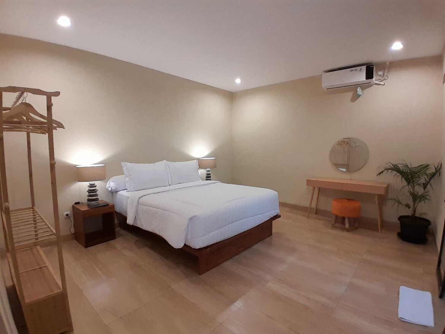 Quarto com cama, mesas de cabeceira com luminárias, escrivaninha, ar condicionado e um cabideiro.