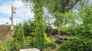 Um jardim com um banco de madeira, um banco de pedra e um comedouro de pássaros em um poste de madeira.