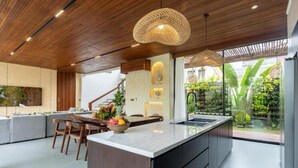Uma cozinha moderna com uma ilha grande, teto de madeira e vista para um jardim exuberante.