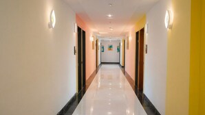 Um corredor de hotel com piso lustroso, luminárias fixadas na parede e quadros decorativos.