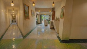 Um corredor de hotel com piso ladrilhado, iluminação pendente, obras de arte emolduradas e um balcão de recepção.
