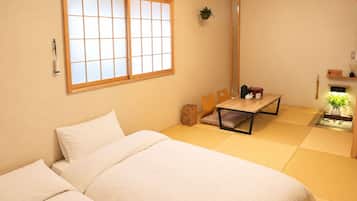 Quarto com cama, mesa, cadeiras, uma pequena planta e janela com vista.