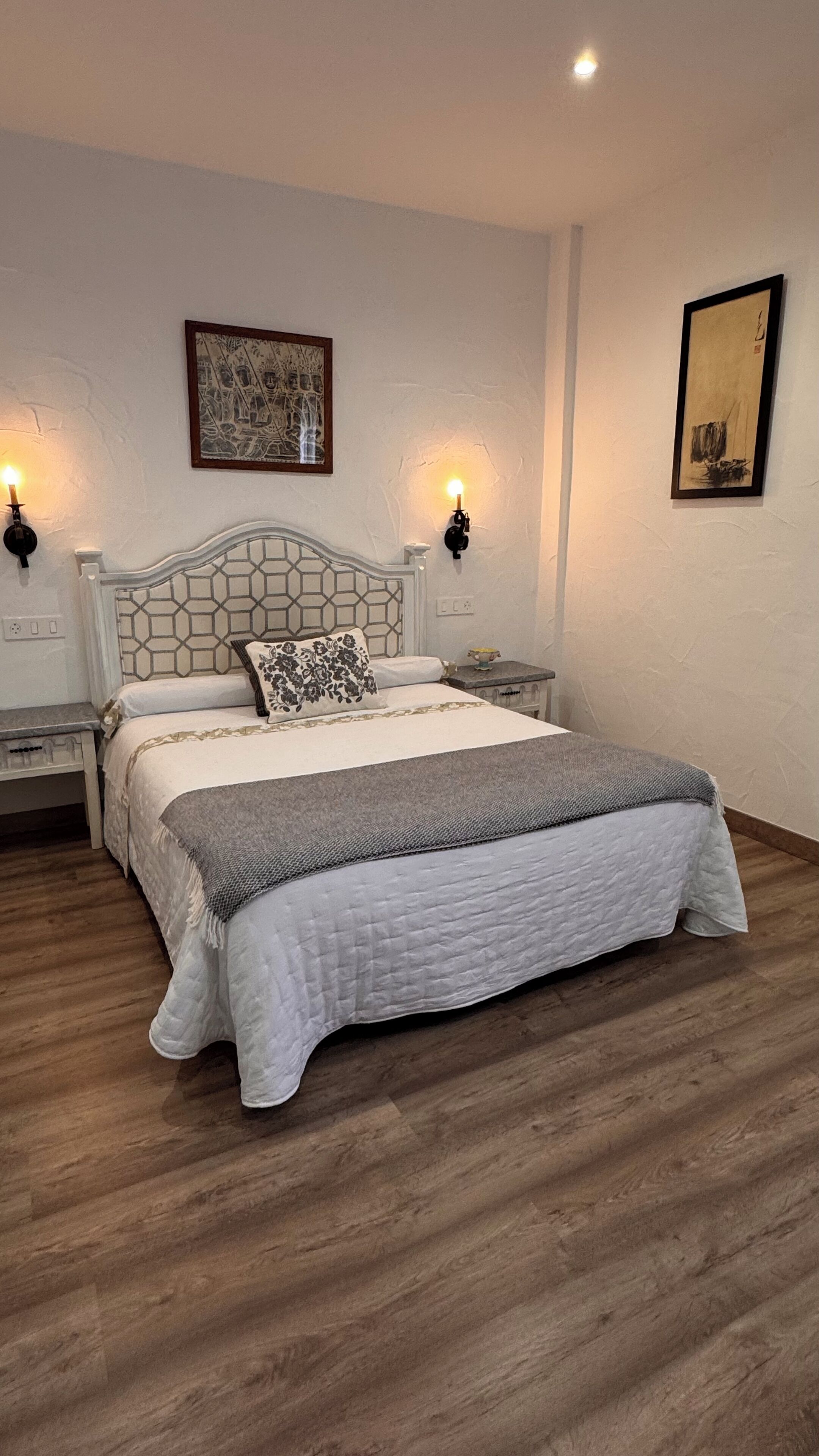 Quarto bem arrumado com uma cama, duas mesas de cabeceira e duas luminárias fixadas na parede.