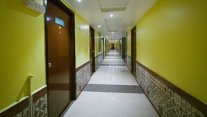 Um corredor de hotel com paredes amarelas, piso de azulejos e portas dando acesso aos quartos.