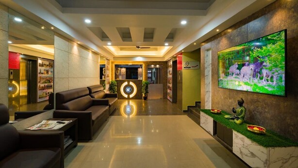 Um lobby moderno com balcão de recepção, área de estar e uma grande televisão exibindo uma paisagem natural.