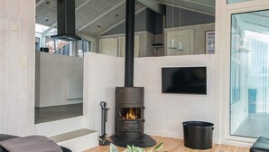 Uma sala de estar moderna com uma lareira a lenha, uma TV de tela plana e uma janela grande.