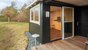 Um edifício moderno com fachada escura, deck de madeira e porta de vidro que dá para um espaço com interior em madeira.
