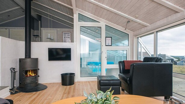 Uma sala de estar moderna com uma lareira a lenha, televisão e uma grande janela com vista para uma piscina.