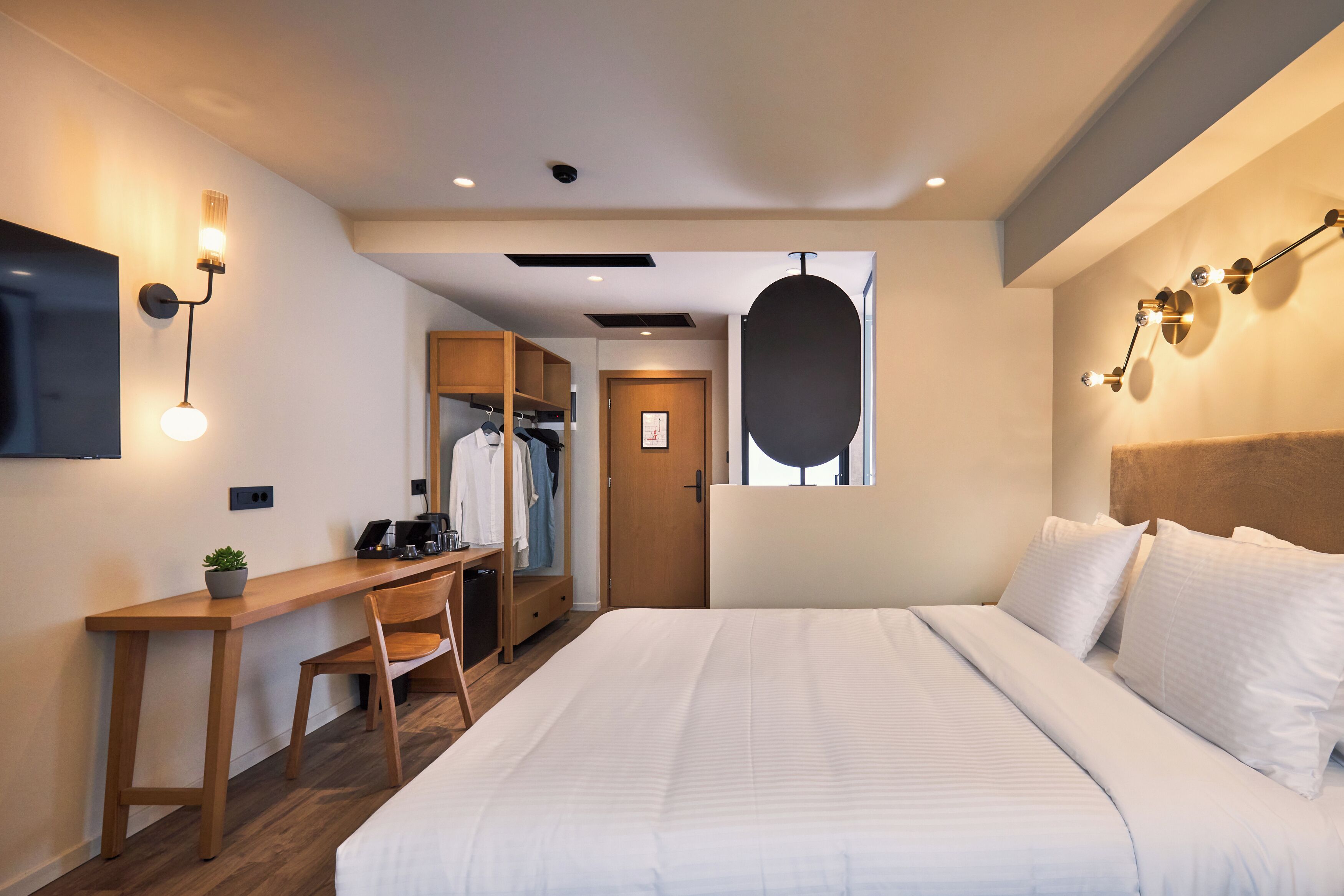Quarto de hotel moderno com cama, escrivaninha, cadeira e guarda-roupa.