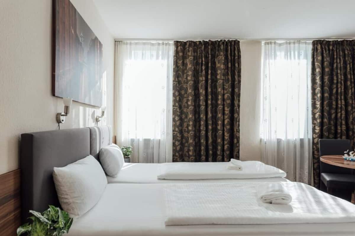 Quarto de hotel com duas camas, um quadro grande na parede e um espaço de refeições com mesa e cadeiras.