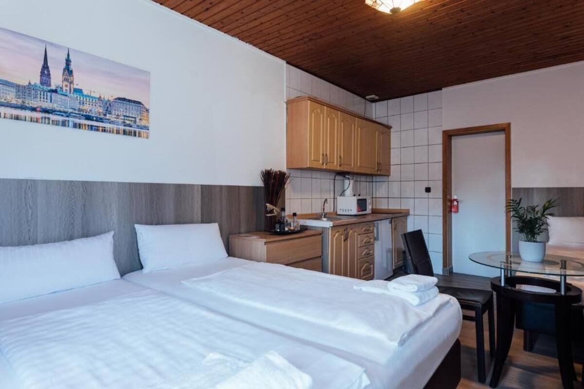 Quarto de hotel com cama grande, pequeno espaço de cozinha, mesa de jantar e vista para a paisagem urbana.