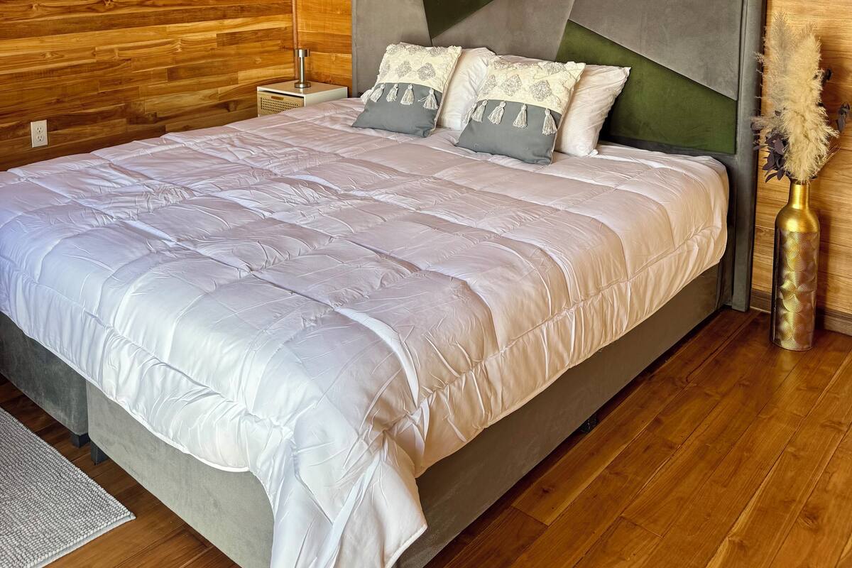 Quarto moderno com parede de madeira, uma cama grande com roupa de cama branca e um vaso decorativo.