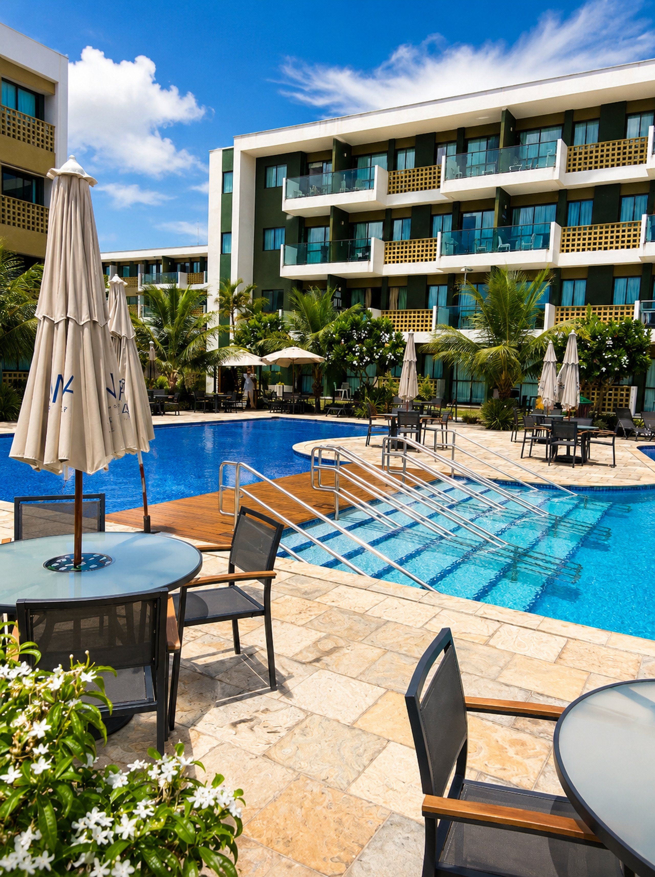 Uma área de piscina de hotel com várias espreguiçadeiras e guarda-sóis, cercada por um edifício com vários andares e varandas.