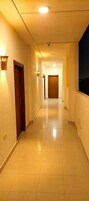 Um corredor longo e bem iluminado, com pisos em azulejo e portas em ambos os lados.