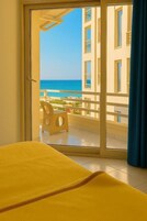 Quarto de hotel com porta de vidro deslizante para uma varanda com vista para o oceano.