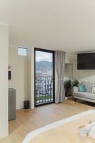 Quarto de hotel moderno com varanda, sofá, televisão e vista da cidade.