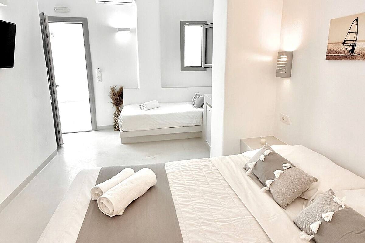 Quarto de hotel moderno com uma cama grande, um espaço de estar e vista para a praia.
