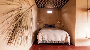 Quarto com uma cama, luminária pendente e uma planta grande.