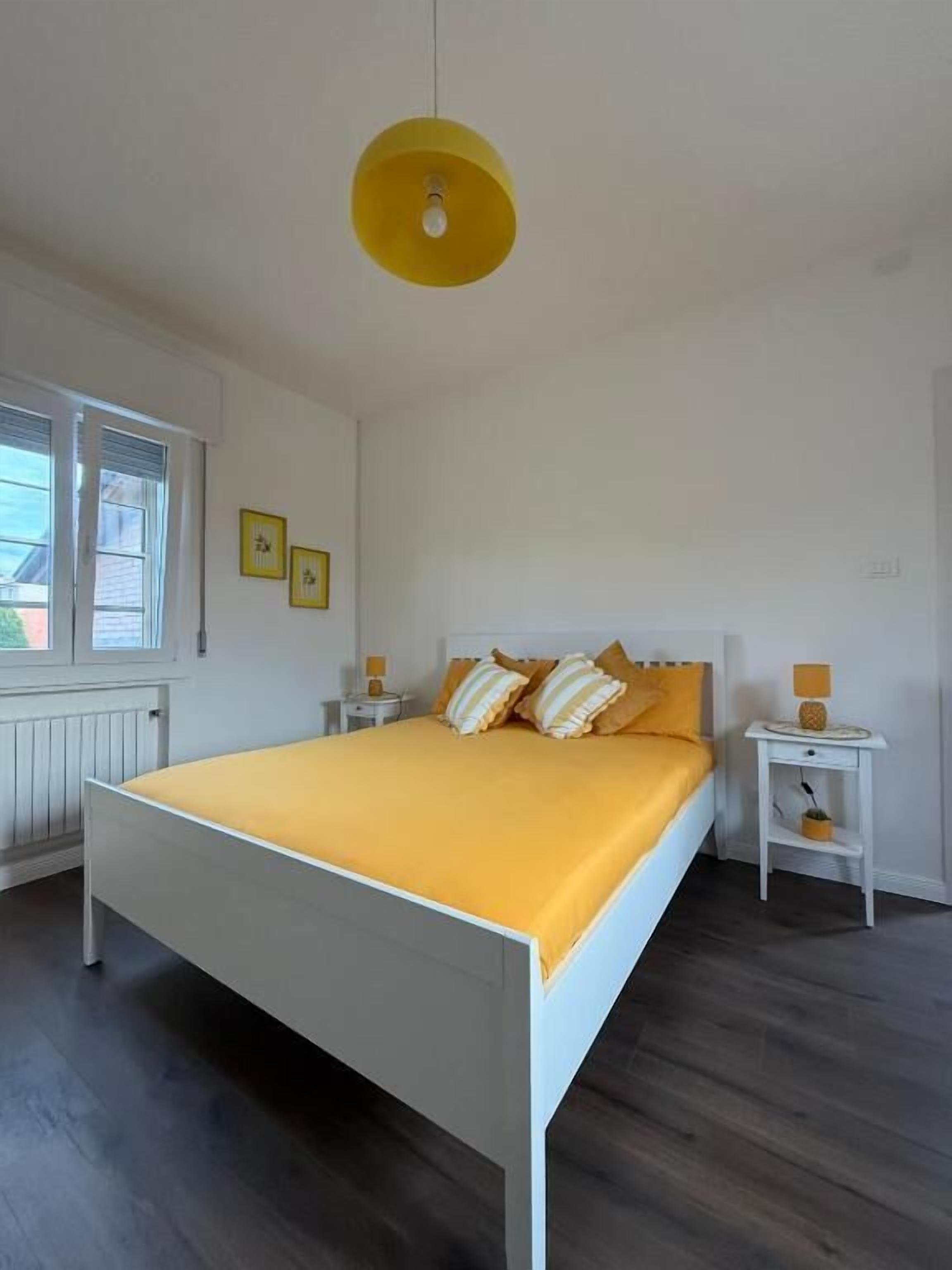 Um quarto com uma cama, uma mesa de cabeceira, uma luminária e uma janela.
