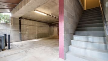 Escadaria de concreto que desce a um andar inferior, com corrimão de metal e luminária fluorescente.