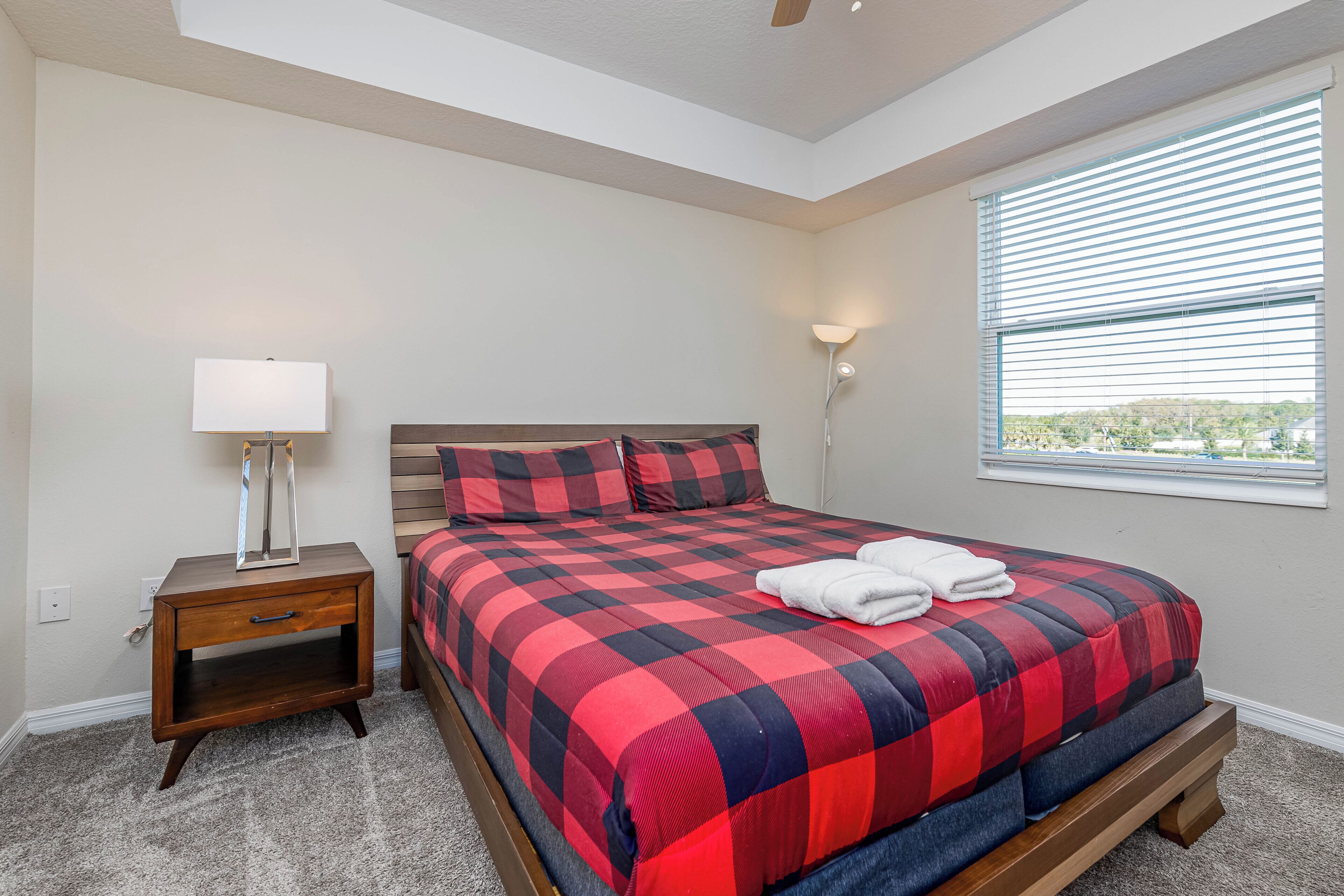 Quarto com cama, mesa de cabeceira, abajur e janela.