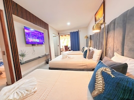 Quarto de hotel com duas camas, televisão na parede, mesa de cabeceira e uma janela grande com cortinas.