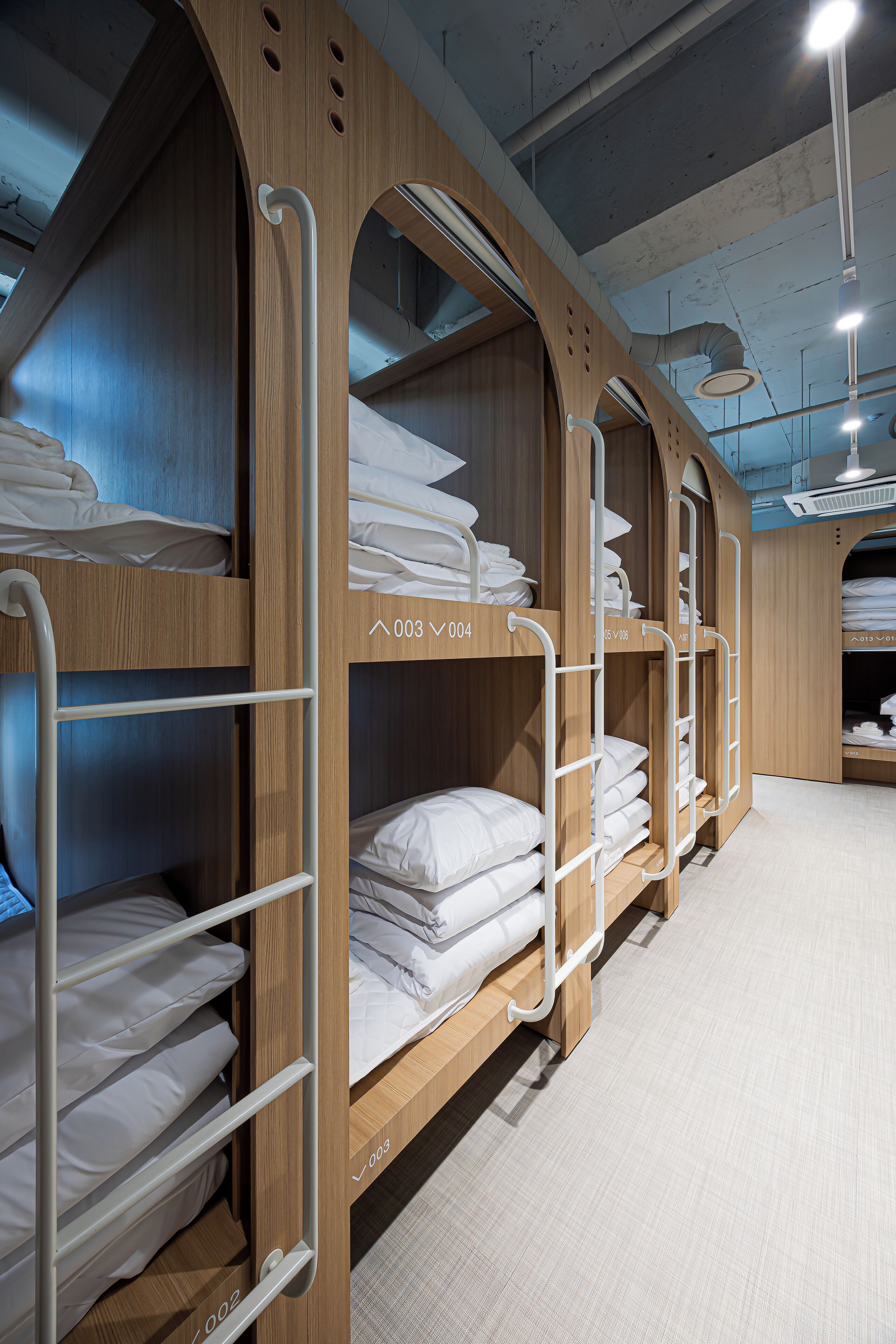 Beliches com roupa de cama branca, grades de madeira e um chão limpo revestido de azulejos.